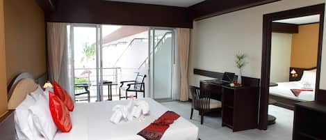 Quarto de hotel com uma cama grande, uma escrivaninha e uma cadeira. Tem uma varanda com vista para palmeiras e um edifício.