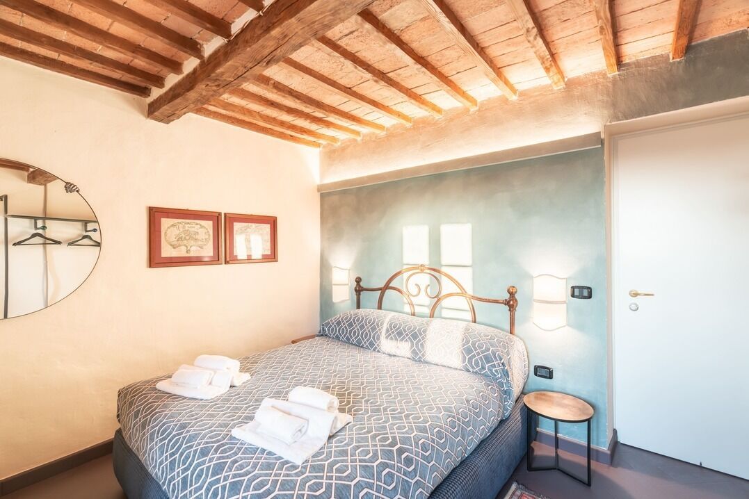 Quarto com cama, mesa de cabeceira, espelho e luzes na parede.