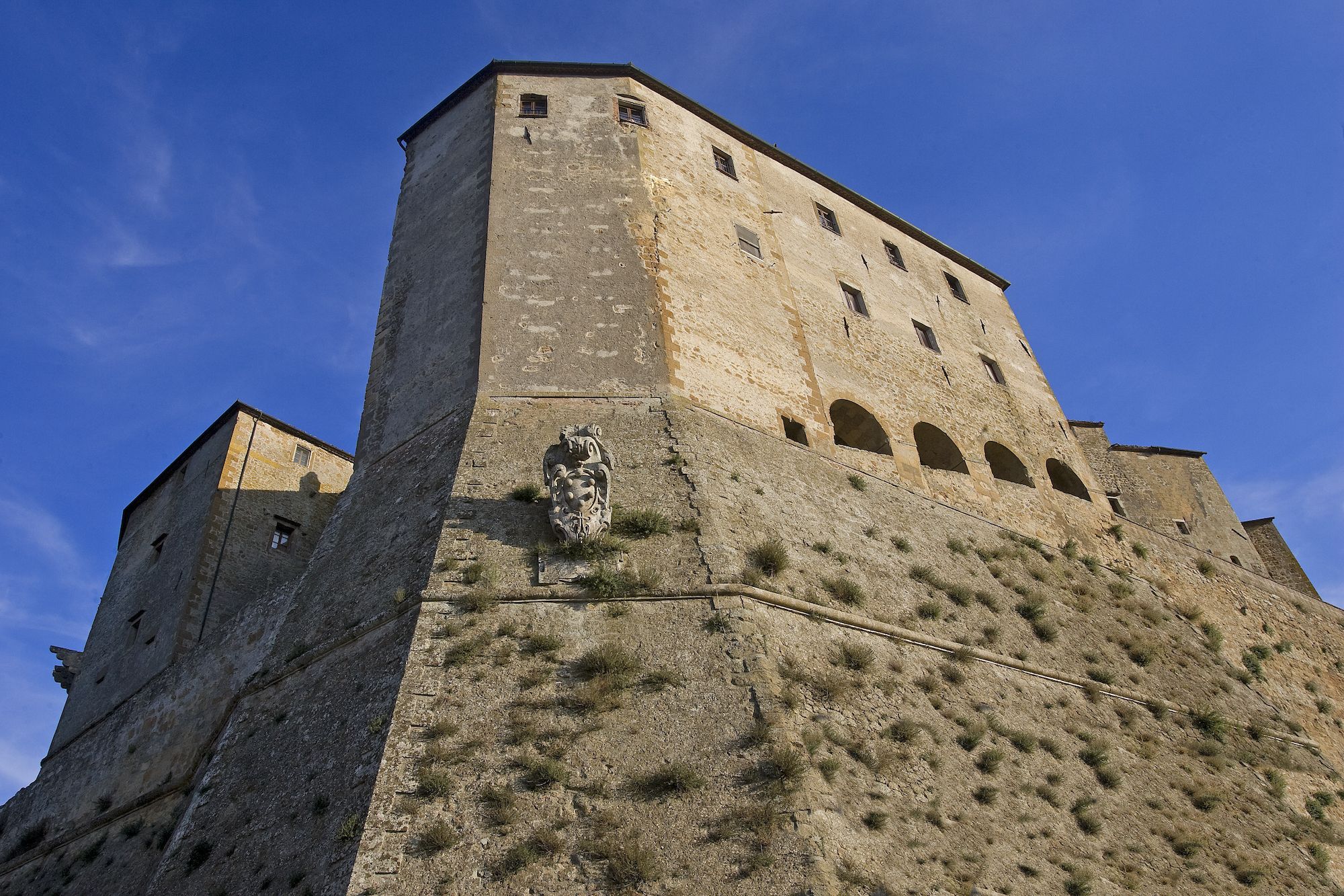 Um edifício histórico de pedra com uma torre imponente, janelas em arco e um brasão.