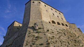 Um edifício histórico de pedra com uma torre imponente, janelas em arco e um brasão.