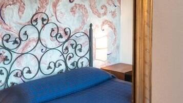 Quarto com cama, mesa de cabeceira e parede com padrão floral.