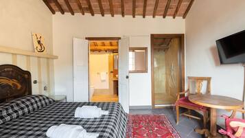 Quarto de hotel com cama, poltrona, mesa e televisão.