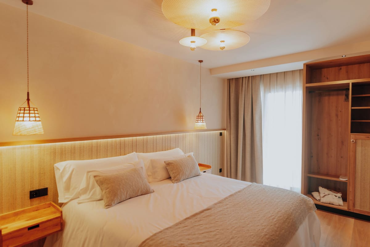 Quarto de hotel com cama grande, cabeceira de madeira, mesas de cabeceira e guarda-roupa.