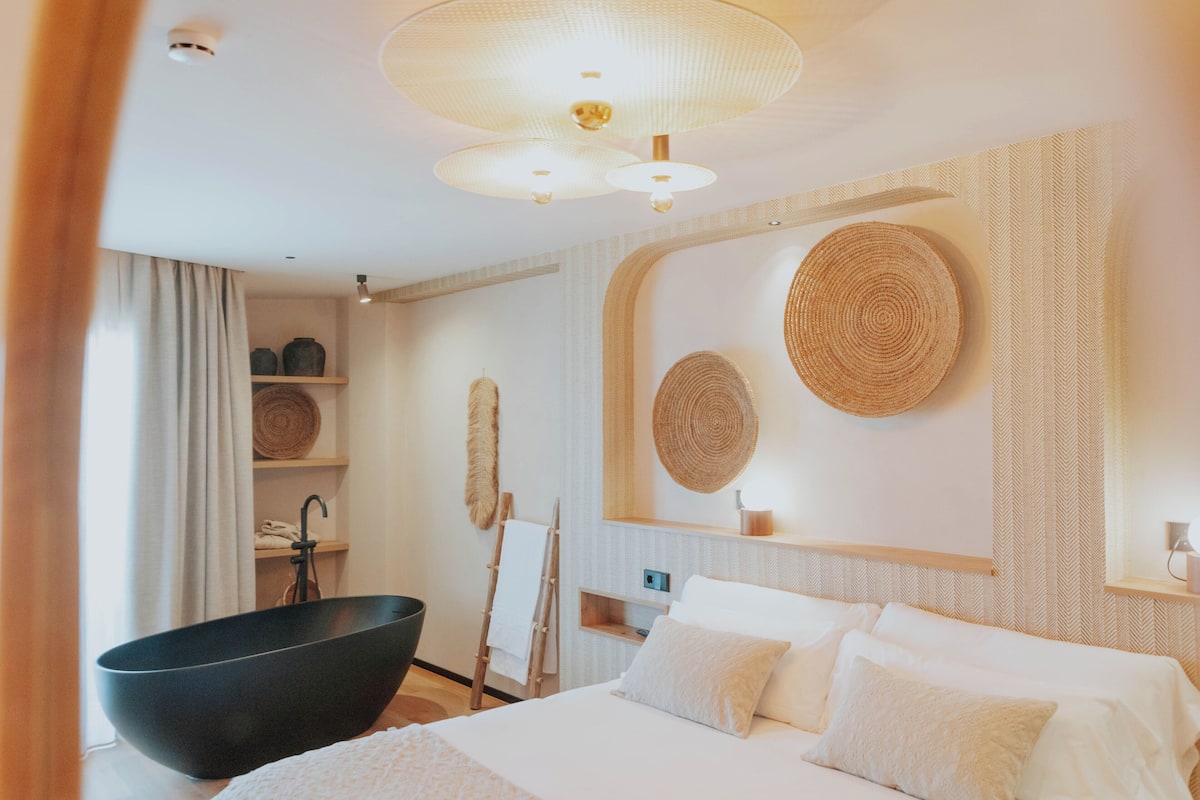 Quarto de hotel moderno com uma cama grande, uma banheira preta e uma escada de madeira.