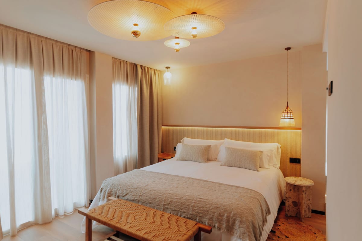 Quarto com uma cama grande, mesa de cabeceira, luminária pendente e janela com cortinas.
