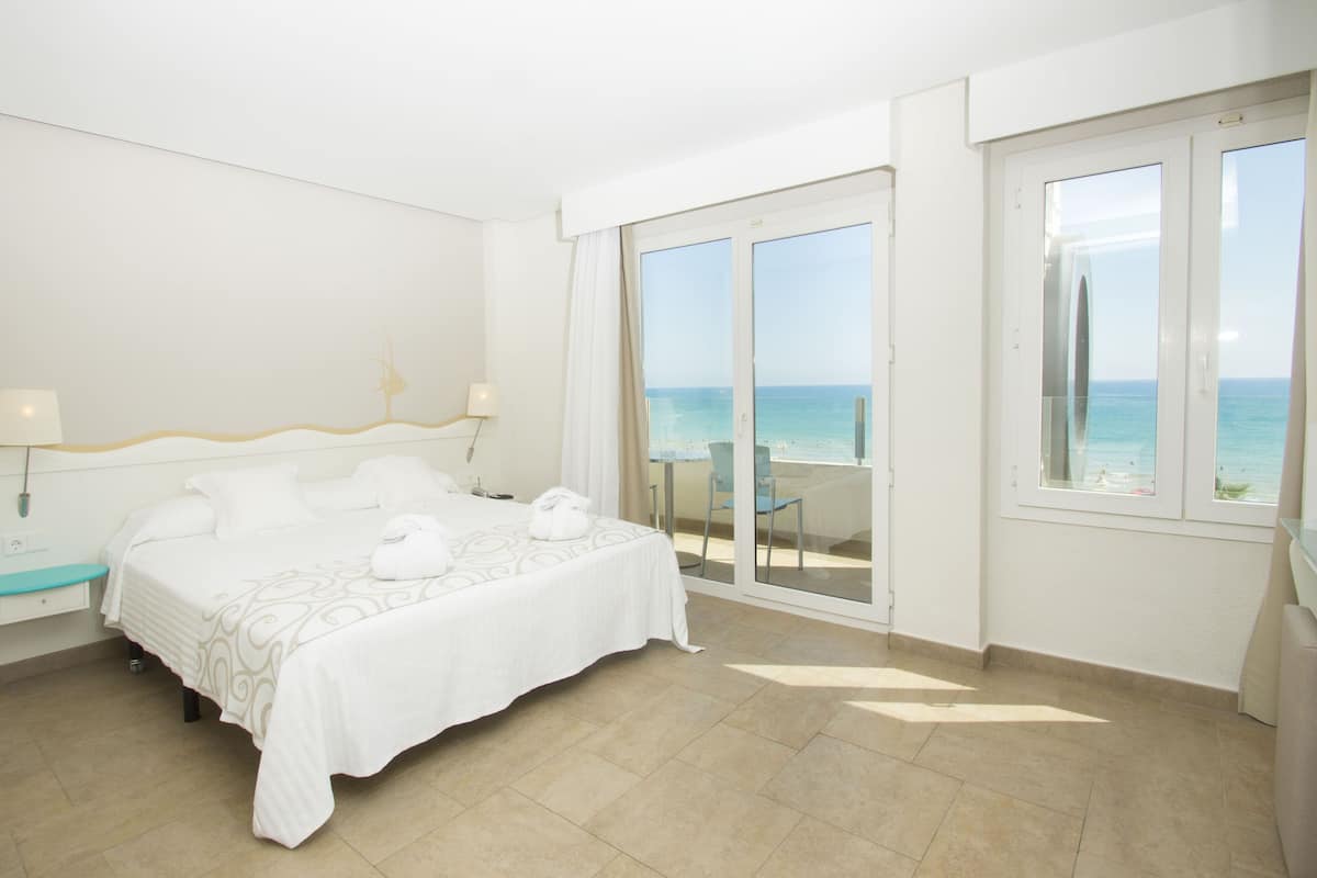 Quarto de hotel com uma cama, uma escrivaninha, uma cadeira e vista para o oceano.