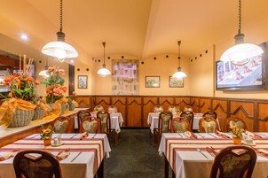 Um restaurante com várias mesas preparadas para refeições, com cestos de vime com flores, cadeiras de madeira e luminárias pendentes.