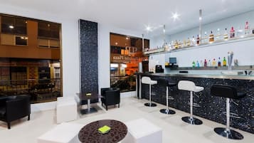 Uma área de bar moderna com balcão de vidro, banquetas e diversas garrafas.