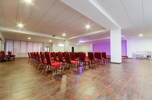 Um salão amplo com fileiras de cadeiras vermelhas, piso de azulejos e parede iluminada em roxo.