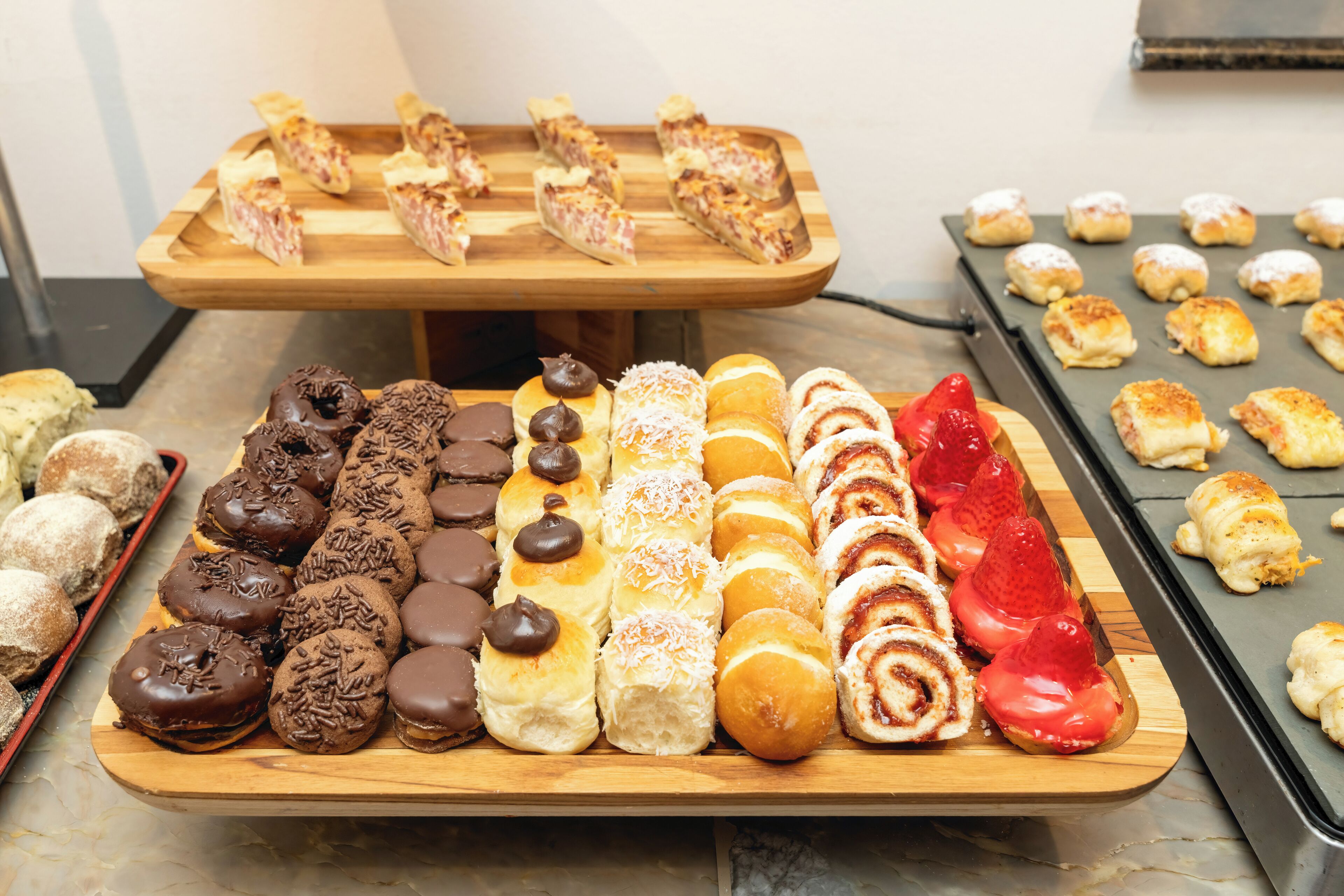 Diversos pastéis e sobremesas em bandejas de madeira.