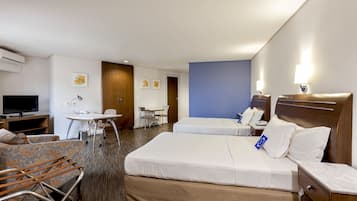 Quarto de hotel com duas camas, uma escrivaninha, uma cadeira, uma televisão e uma mesinha.