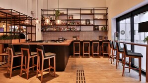 Uma área de bar moderna com banquetas de madeira, prateleiras com garrafas e iluminação pendente.