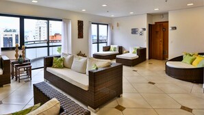 Um hall espaçoso com uma grande janela, um sofá, uma área de estar circular e uma mesa pequena com objetos decorativos.