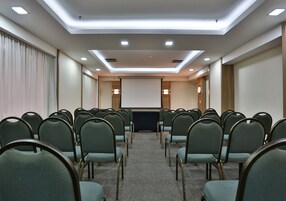 Uma sala de conferências com fileiras de cadeiras, uma tela de projetor e iluminação embutida no teto.