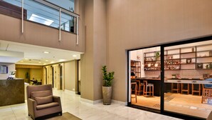 Um hall espaçoso com balcão de recepção, área de estar e vista para um bar através de um painel de vidro.