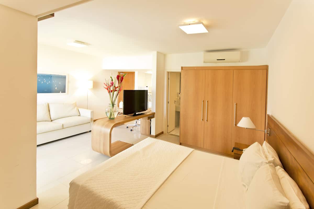 Quarto de hotel com cama, televisão em uma escrivaninha, guarda-roupa e sofá.