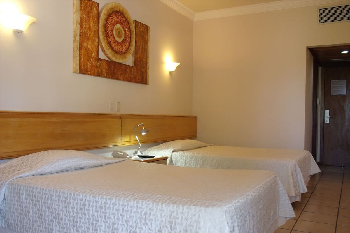 Quarto de hotel com duas camas, um painel de cabeceira de madeira, uma obra de arte pendurada na parede e uma porta.