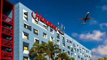 Hotel Hampton by Hilton com céu azul límpido e um avião ao fundo.