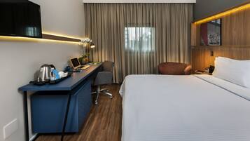 Quarto de hotel com cama, escrivaninha e televisão.