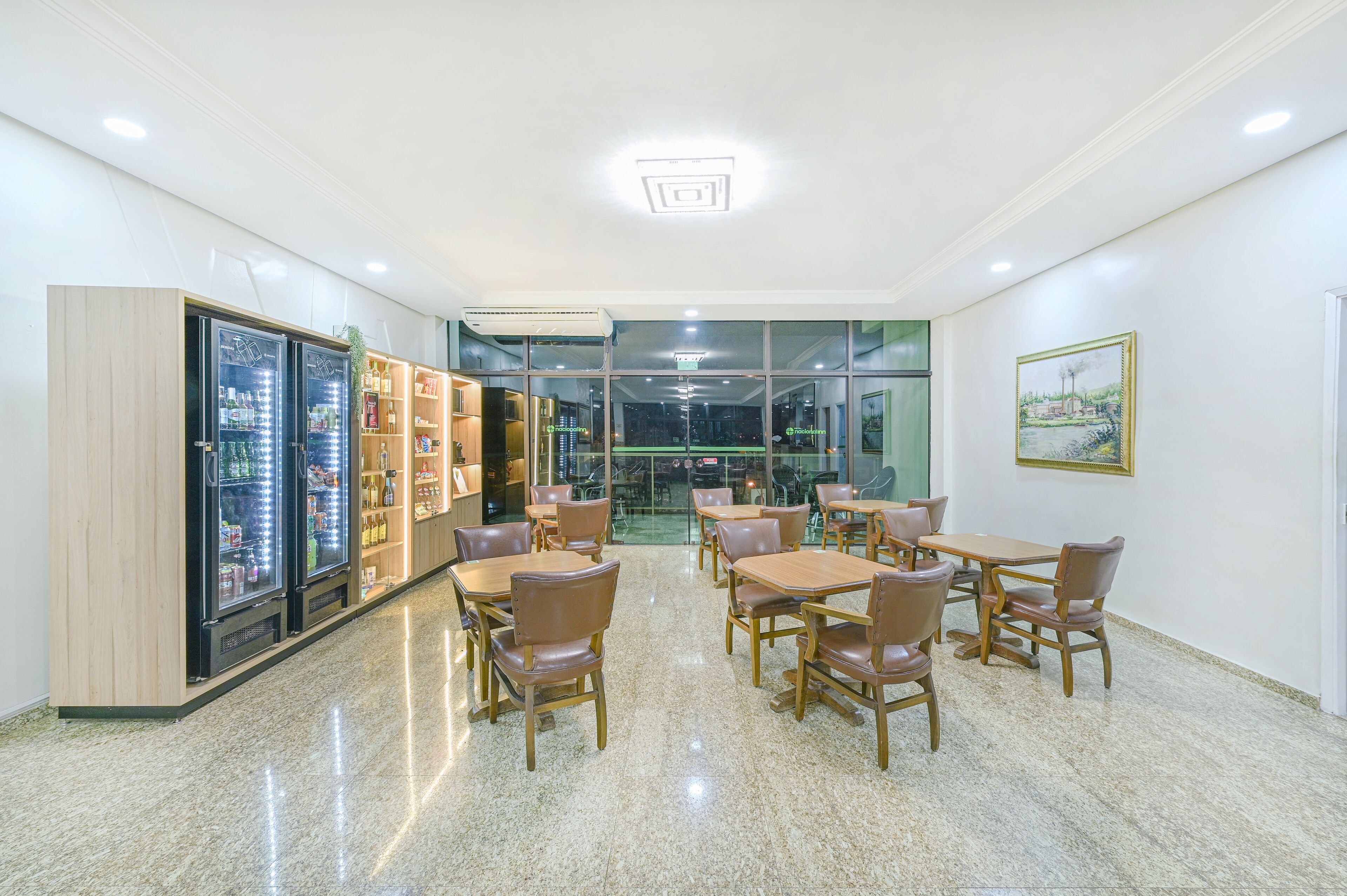 Um espaço interno amplo com piso lustroso, mobiliário de madeira e parede de vidro com vista para o exterior.
