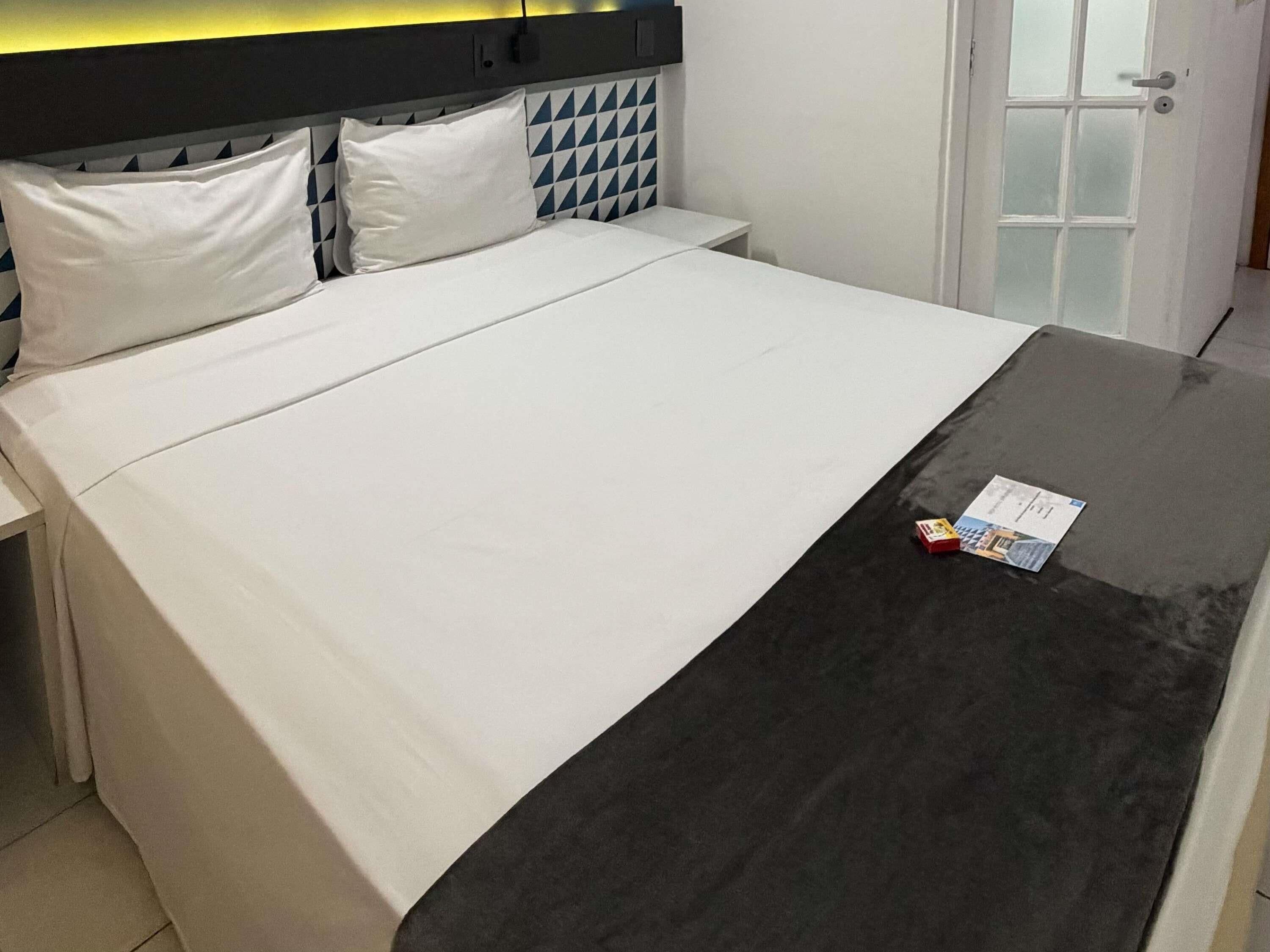 Quarto de hotel com uma cama, mesa de cabeceira e uma porta.
