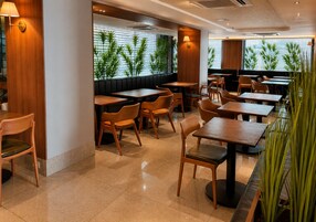 Interior de restaurante com cabines e mesas, cadeiras de madeira e plantas em vasos.