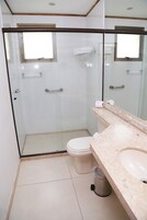 Casa de banho moderna com chuveiro envidraçado, sanita, lavatório e um cesto de lixo.