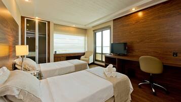 Quarto de hotel com duas camas, uma escrivaninha, uma cadeira, uma televisão e uma janela grande.