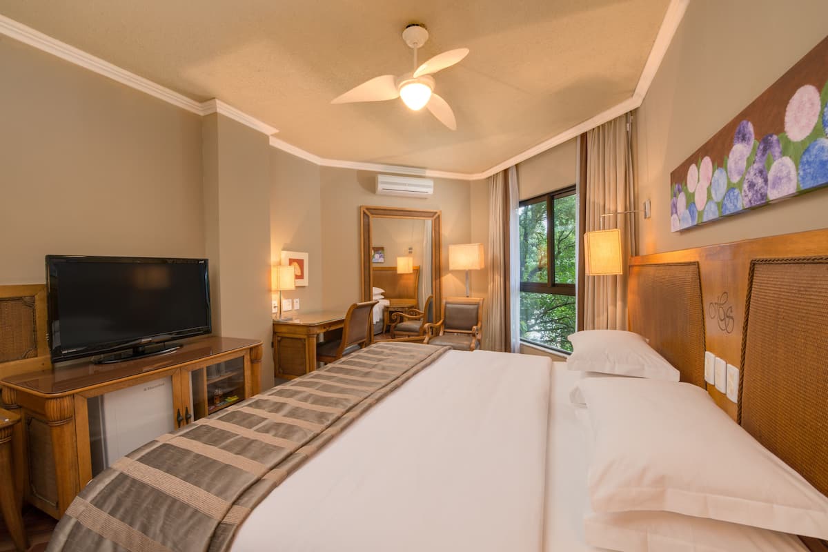 Quarto de hotel com cama, televisão, escrivaninha e cadeira.