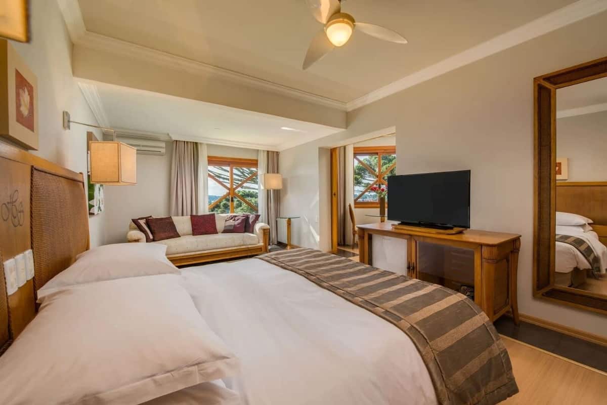 Quarto de hotel com cama grande, sofá, televisão e escrivaninha.