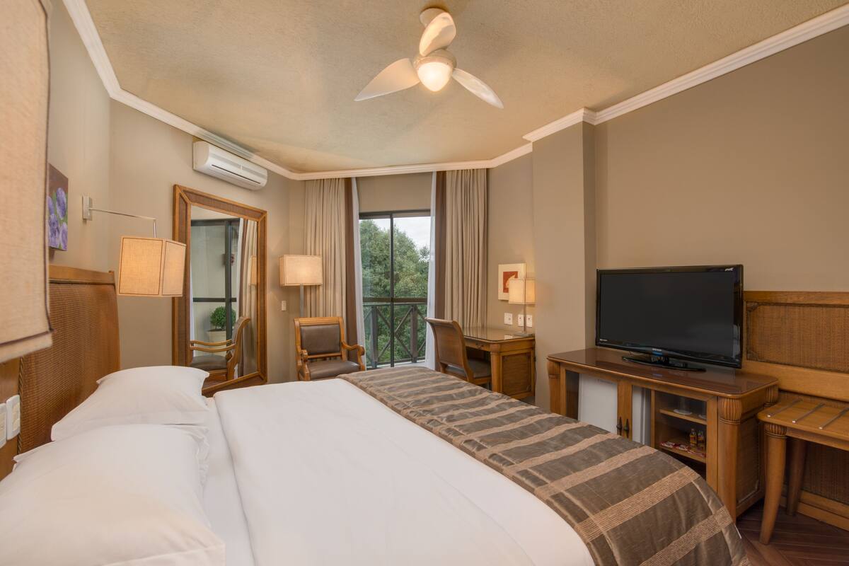 Quarto de hotel com uma cama grande, televisão, escrivaninha e uma cadeira.