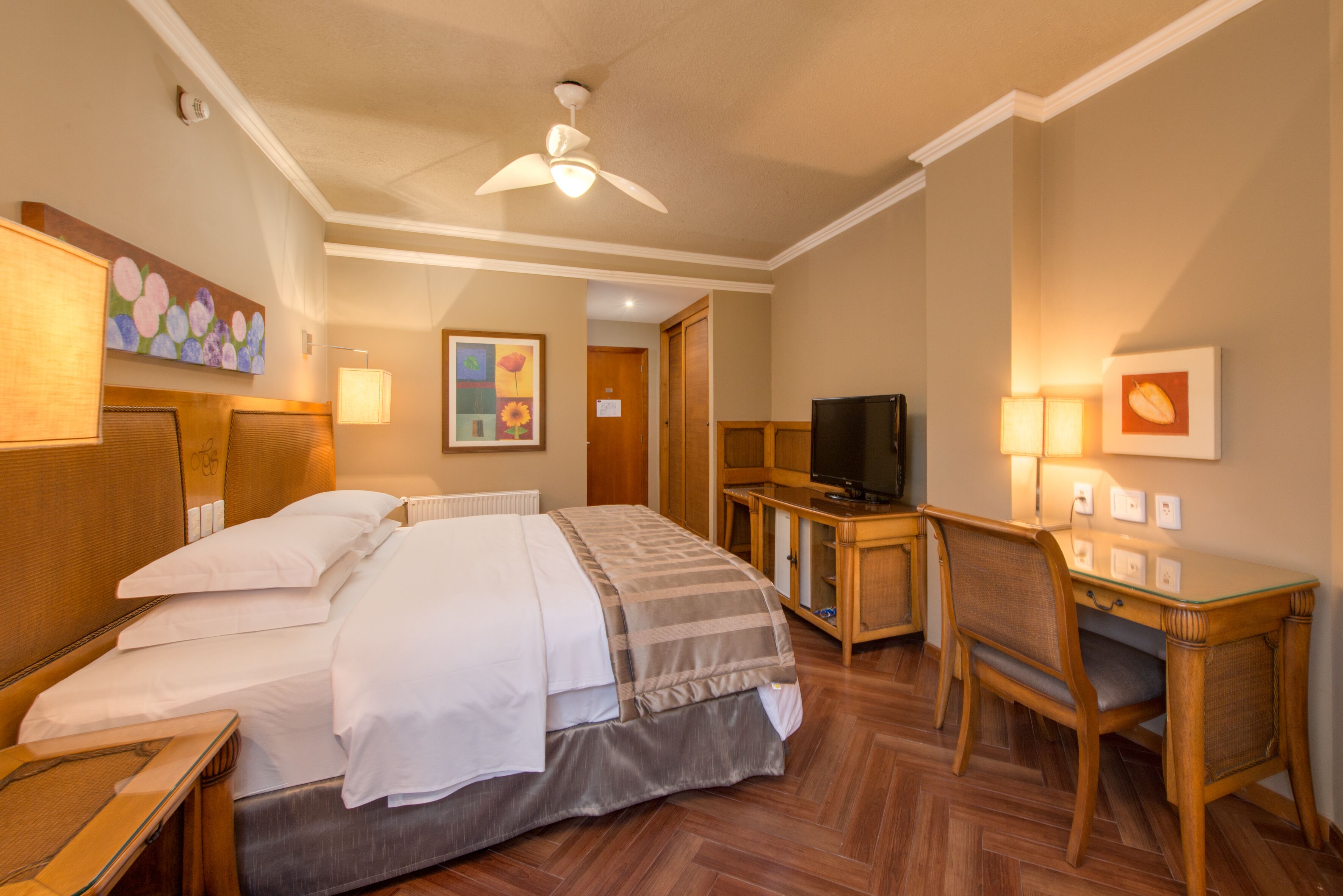 Quarto de hotel com cama, escrivaninha, televisão e obras de arte nas paredes.