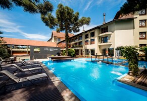 Piscina com espreguiçadeiras, um edifício com a inscrição 'WISH SERRANO' e um céu azul límpido.