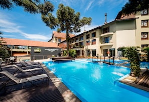 Piscina com espreguiçadeiras, um edifício com a inscrição 'WISH SERRANO' e um céu azul límpido.