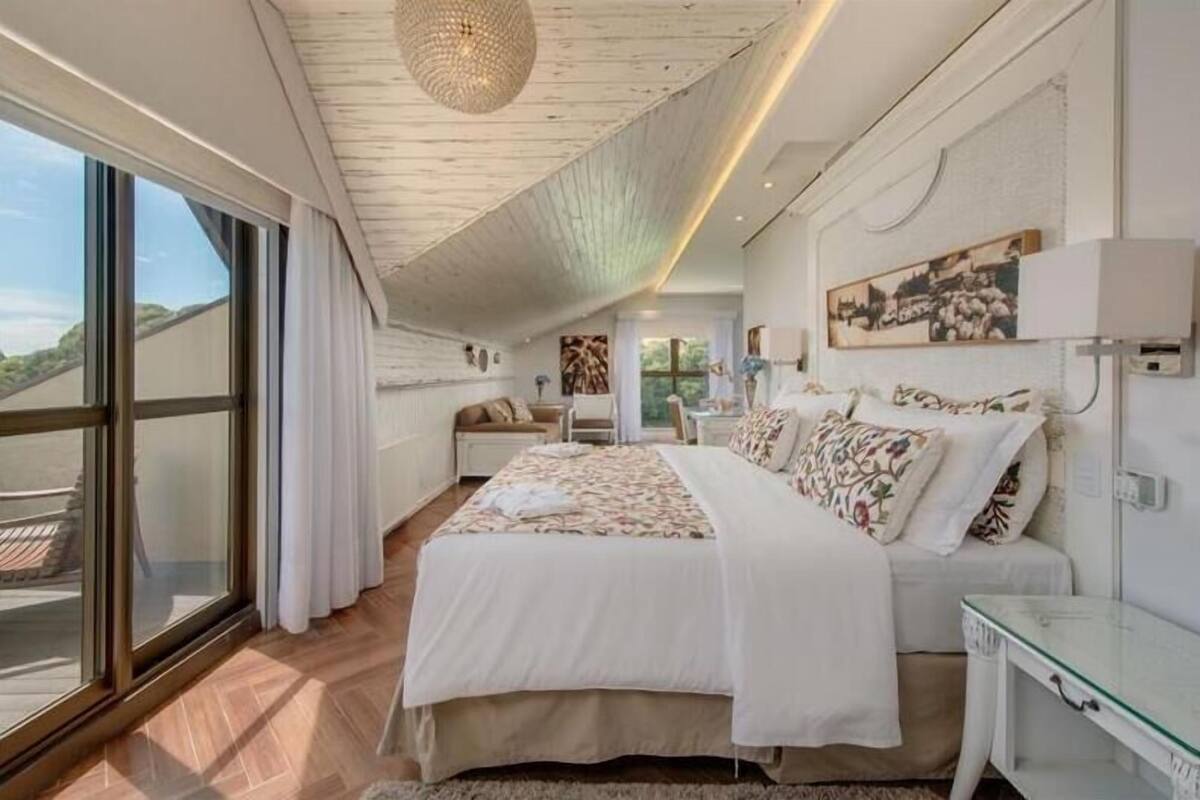 Quarto com uma cama grande, uma mesa de vidro e vista para o exterior.