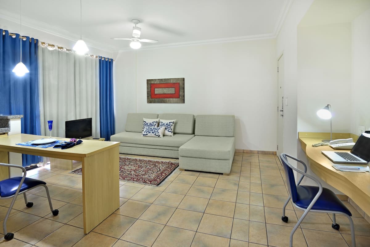 Sala de estar com sofá, escrivaninha, poltrona, televisão e ventilador de teto.
