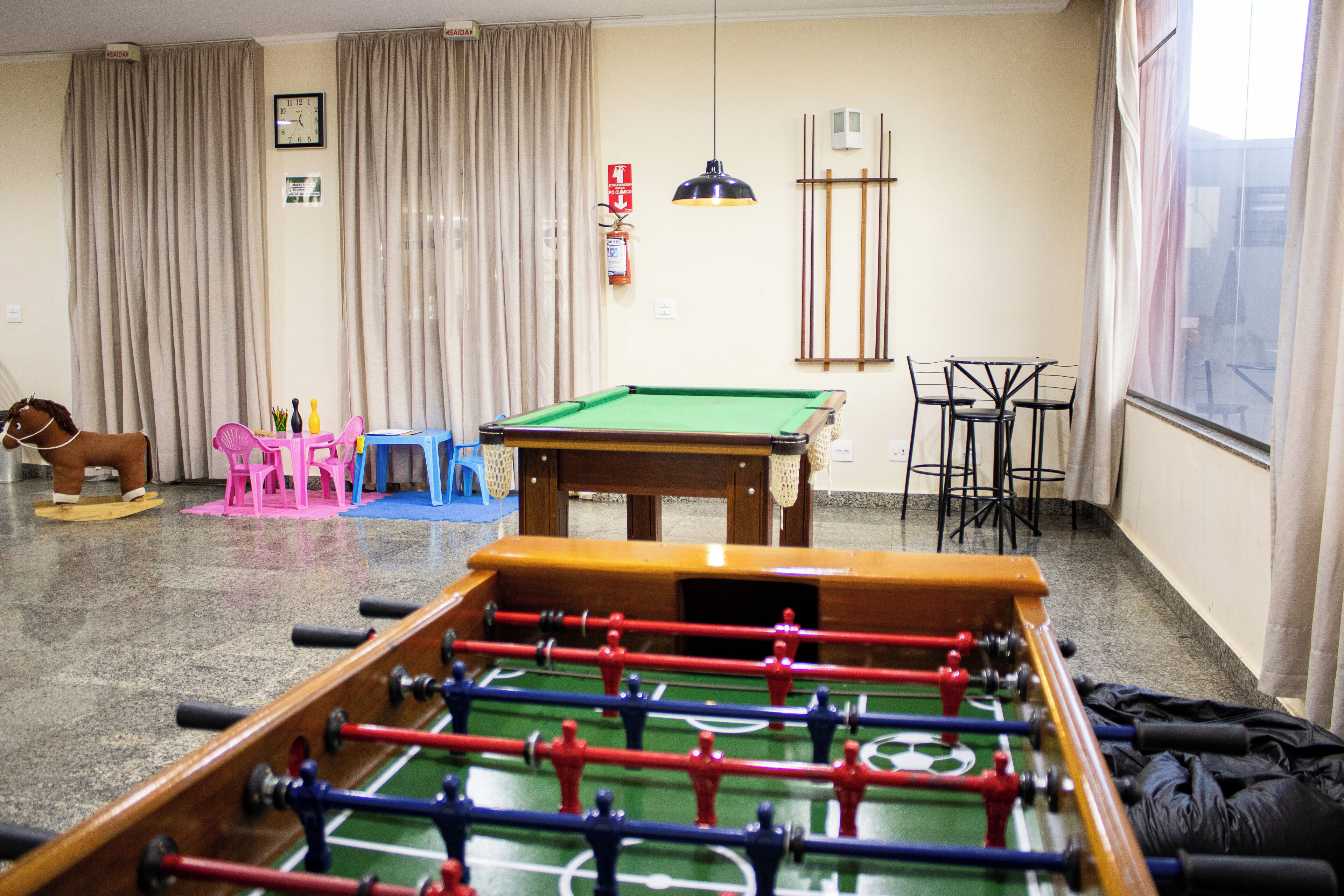 Um quarto com mesa de pebolim, mesa de bilhar e uma janela com cortinas.
