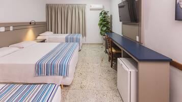 Quarto de hotel com duas camas, uma escrivaninha, uma televisão e uma planta.