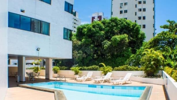 Piscina com espreguiçadeiras, cercada por vegetação e edifícios modernos.