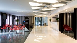 Um lobby moderno com piso refletivo, cadeiras vermelhas, balcão de recepção e design geométrico no teto.