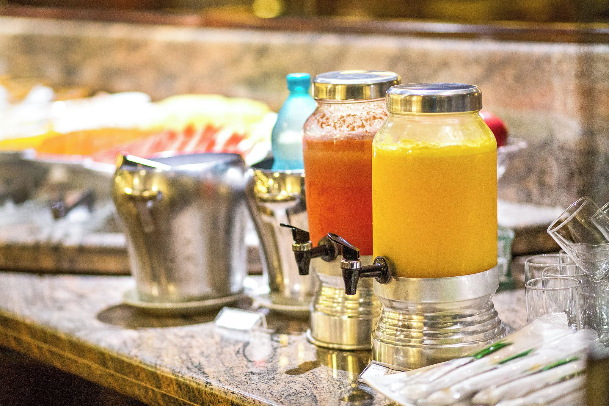 Um balcão de buffet com diversos alimentos e um dispensador de suco.