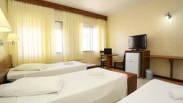 Quarto de hotel com duas camas, uma mesa de trabalho com televisão e uma kitchenette pequena.