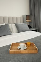 Cama bem arrumada com uma bandeja de itens de café da manhã, incluindo uma xícara de café e um copo de suco de laranja, em um quarto de hotel moderno.