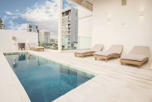 Área de piscina no terraço, com espreguiçadeiras e vista para os edifícios ao redor.