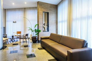 Um saguão de hotel moderno com um sofá de couro, uma mesa redonda, cadeiras, um vaso de planta e uma estátua.