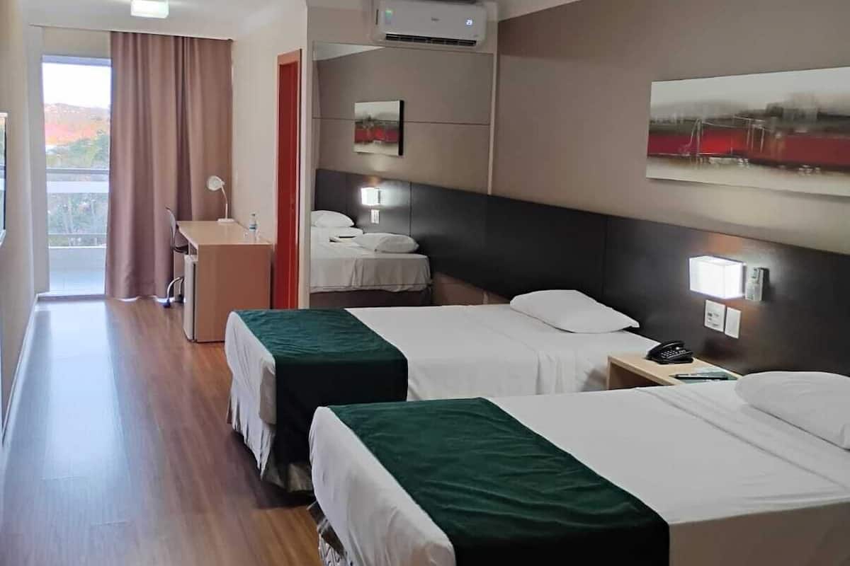 Quarto de hotel com duas camas, uma escrivaninha, uma cadeira, uma mesinha e um quadro na parede.