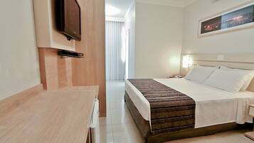 Quarto de hotel com cama, mesa de cabeceira, televisão na parede e um quadro na parede.