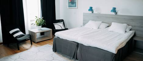 Quarto de hotel moderno com uma cama grande, uma mesa, uma cadeira e um vaso de planta.