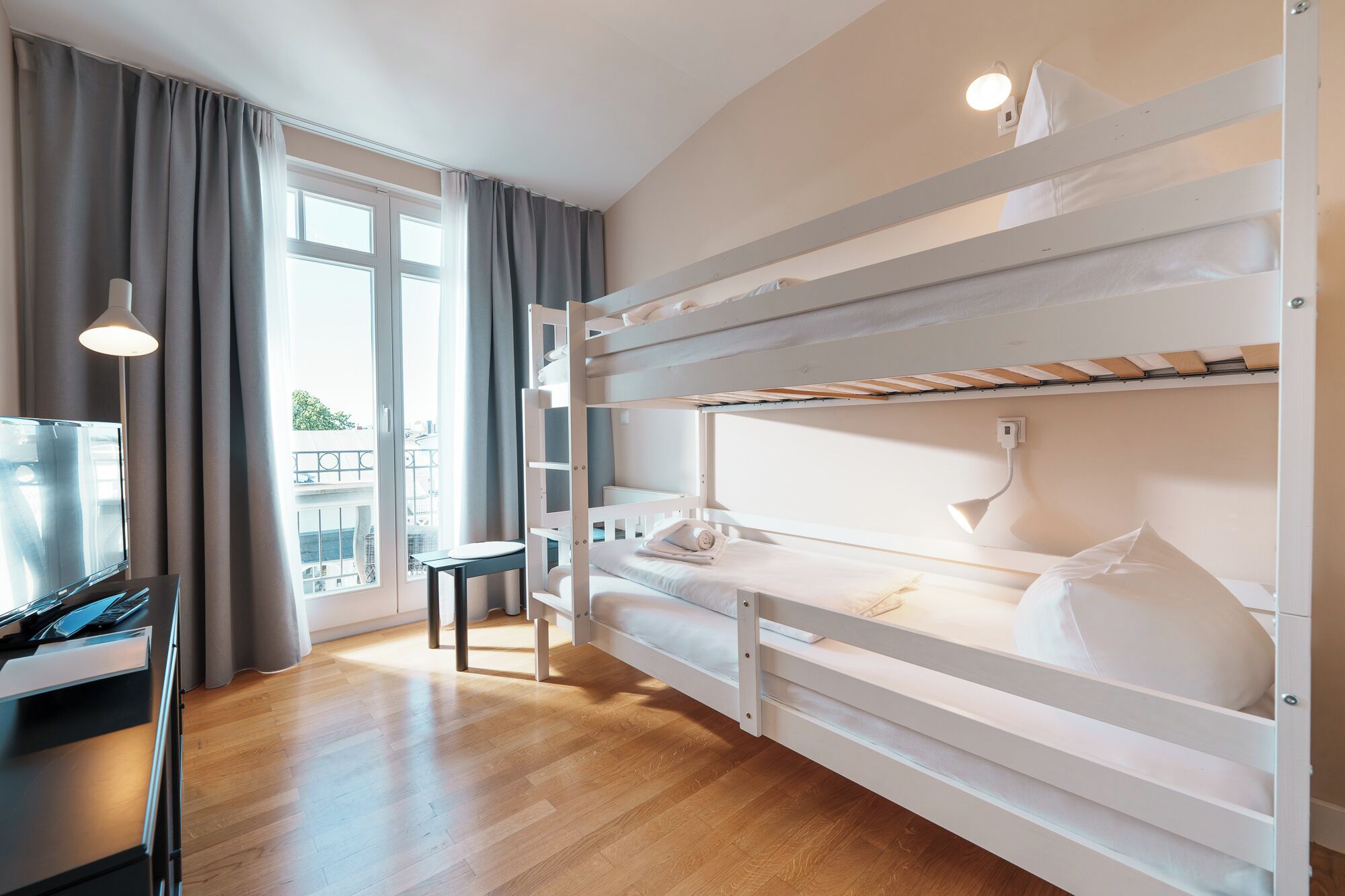 Quarto com beliches, escrivaninha e janela com cortinas.