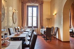 Um restaurante com várias mesas e cadeiras, uma janela grande com cortinas e luminárias fixadas na parede.